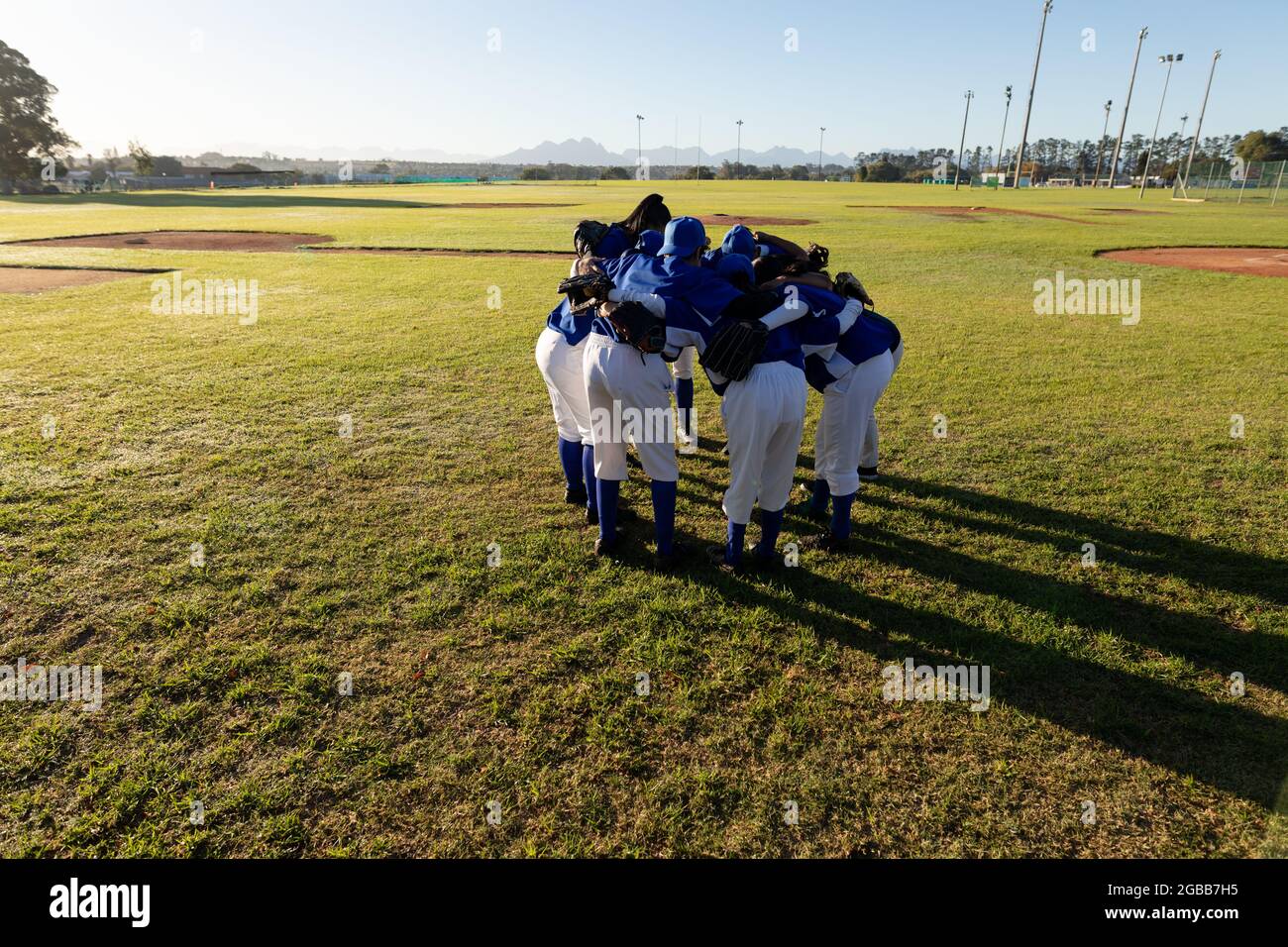 Diverse group of female baseball players standing in huddle on baseball ...
