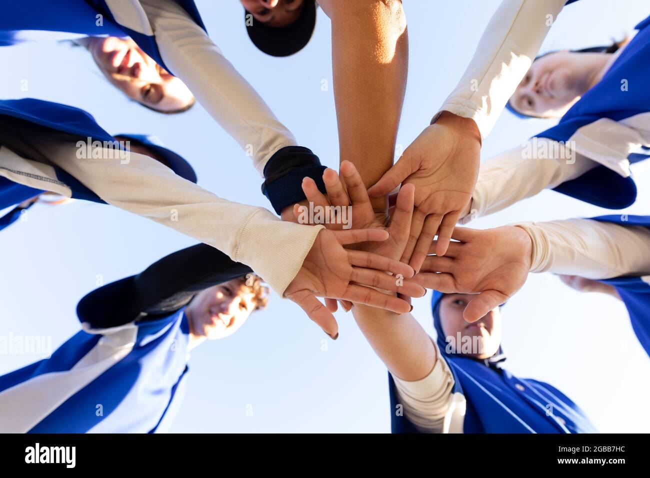Diverse group of happy female baseball players stacking hands on sunny ...