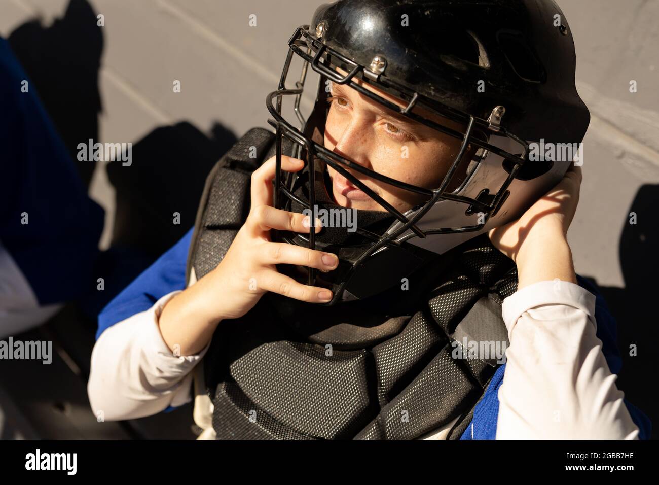 Caucasian female baseball player sitting on bench putting on catcher's ...