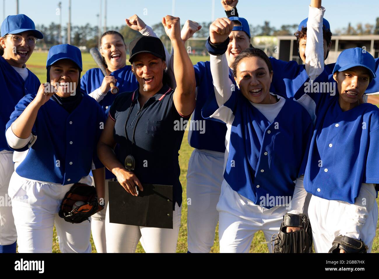Diverse group of happy female baseball players and coach celebrating on ...