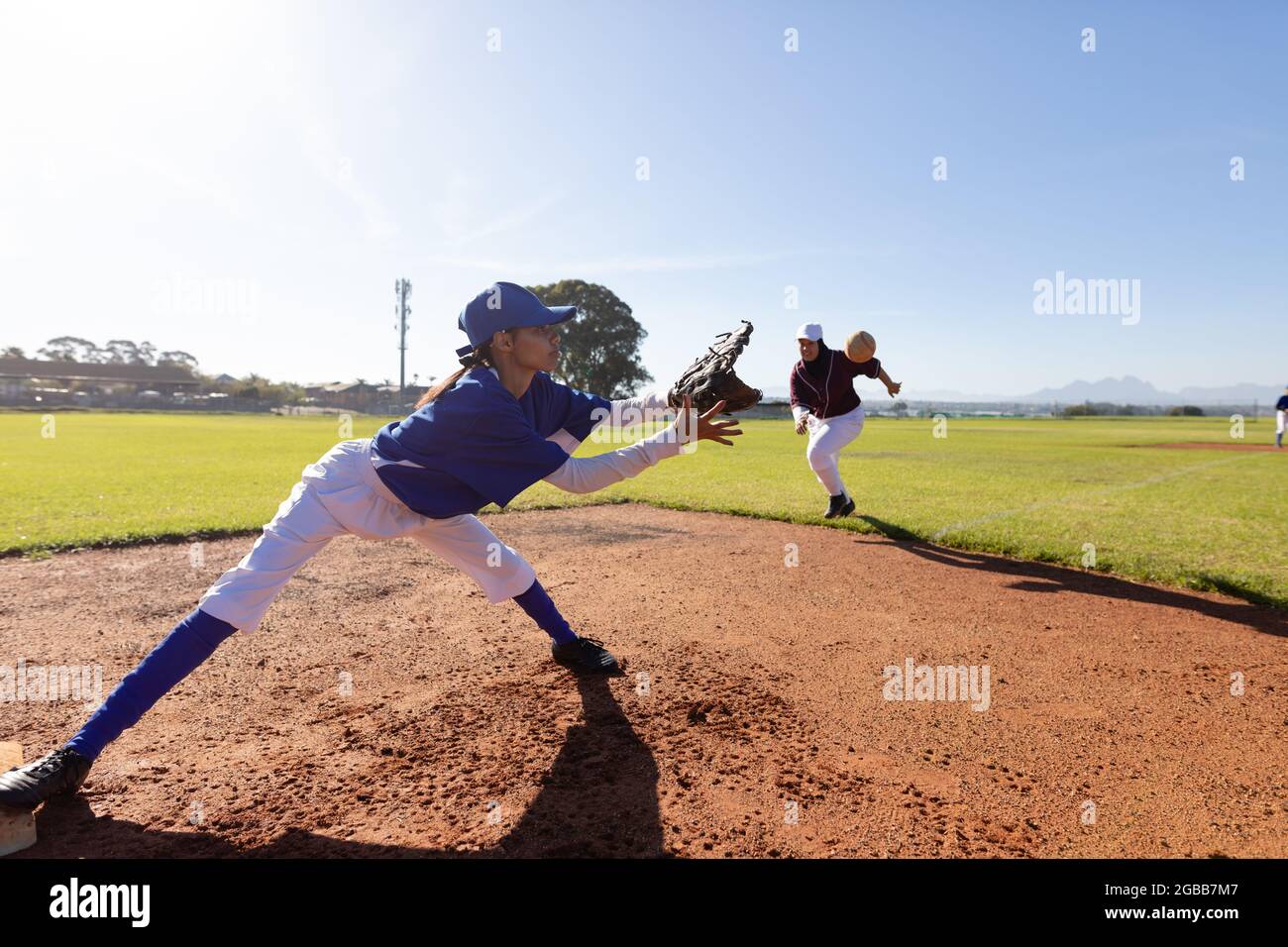 Mixed race female baseball player on sunny baseball field reaching to ...