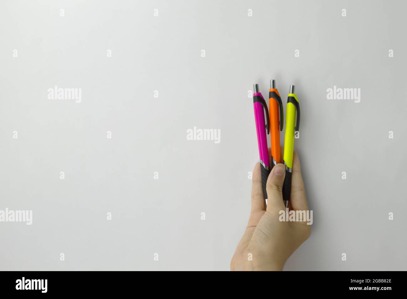hand of a girl holding three pens of a different color on white ...