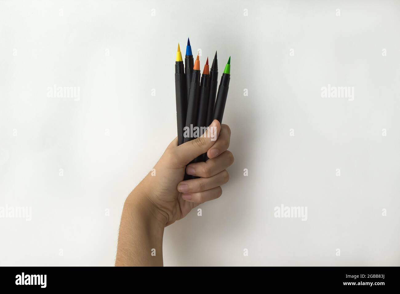 hand of a girl holding a handful of color pens and markers on white ...