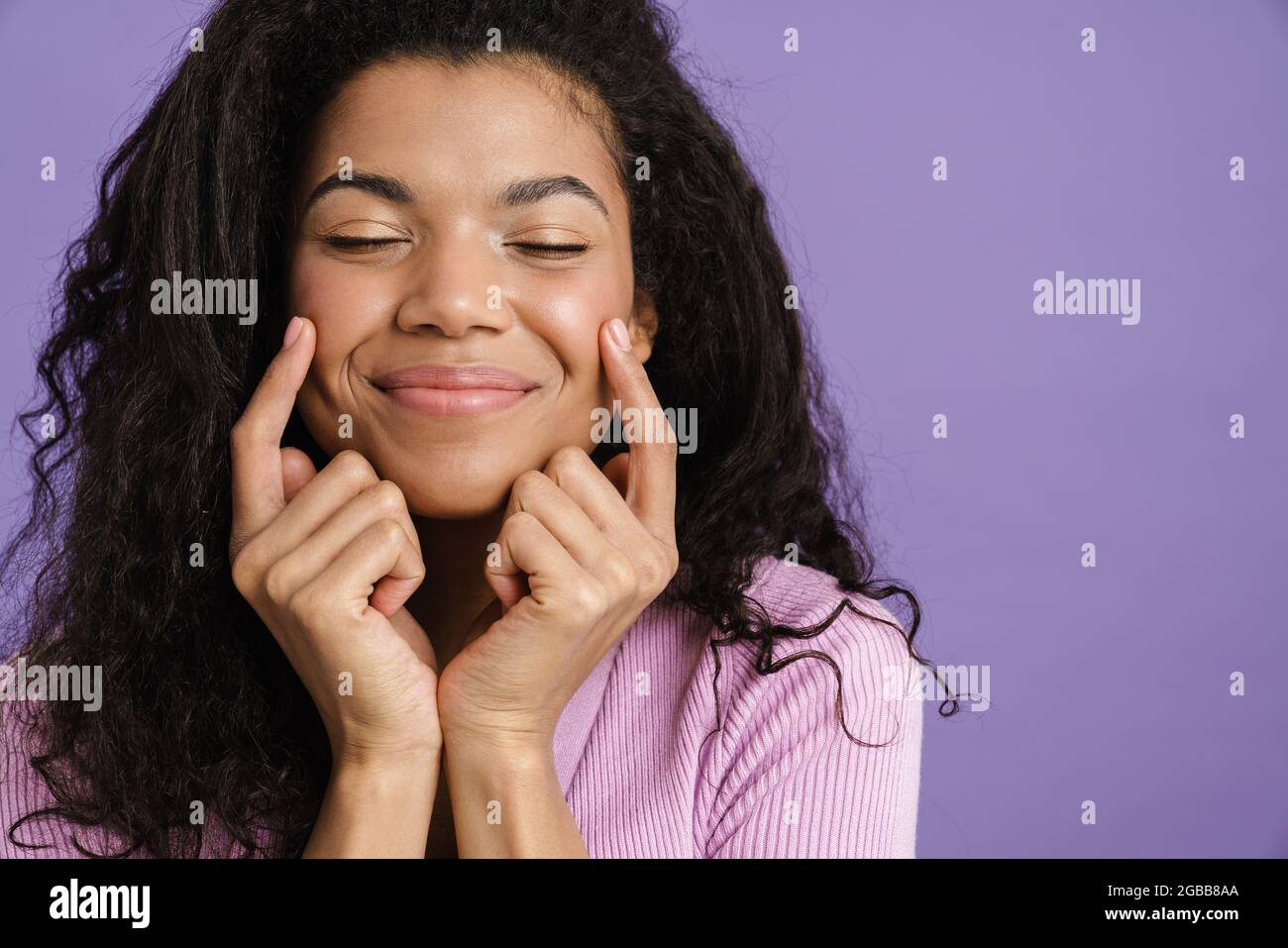 Young black woman smiling and pointing finger at her cheeks isolated ...