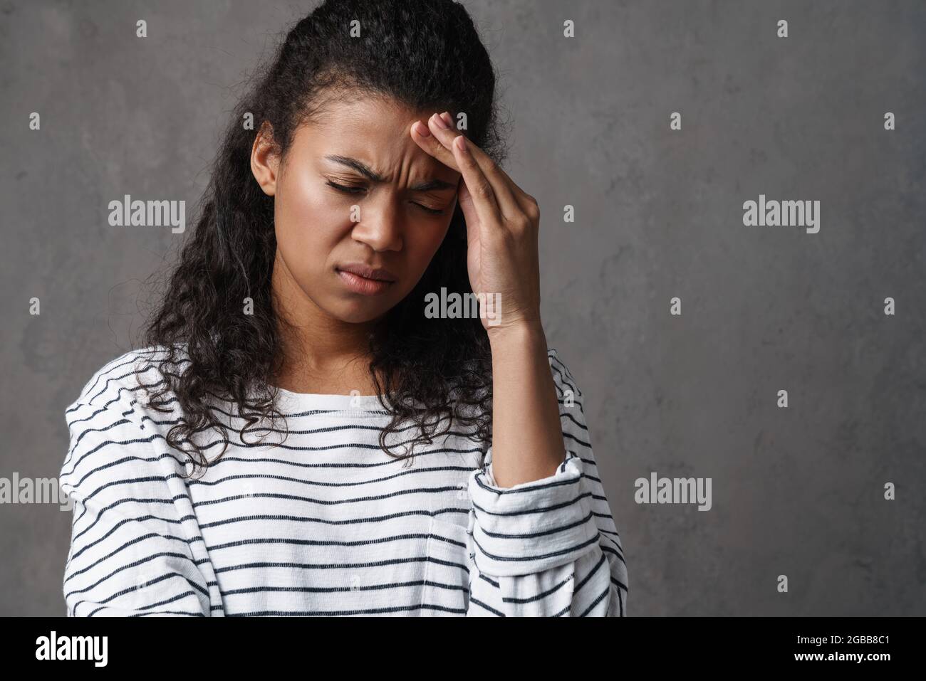 Upset stressed african woman suffering from a headache over gray wall ...