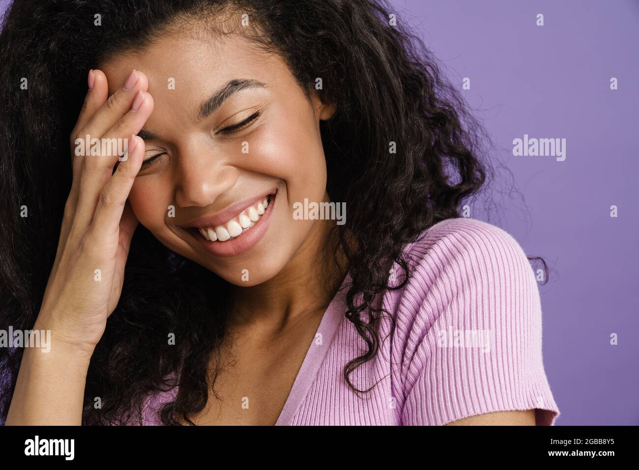 Young black woman laughing and covering her face isolated over purple ...