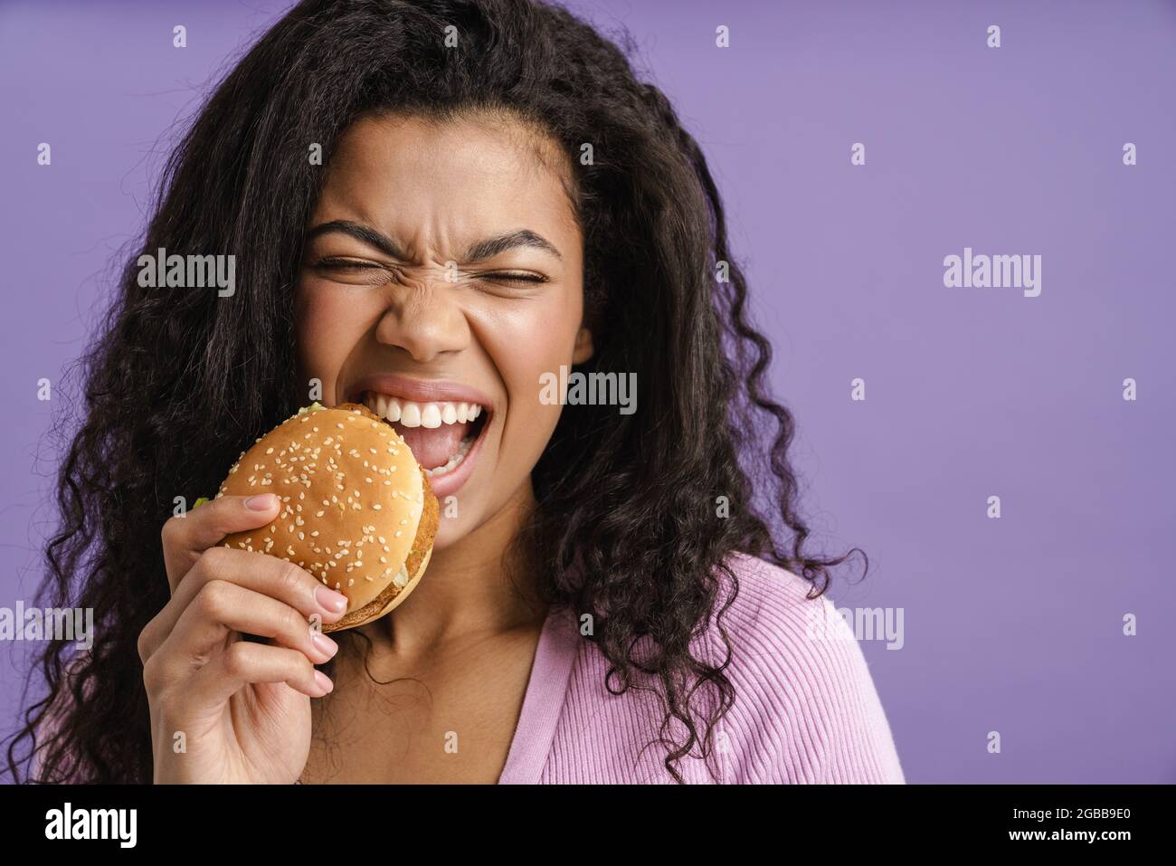 Young black woman with curly hair grimacing while eating hamburger ...