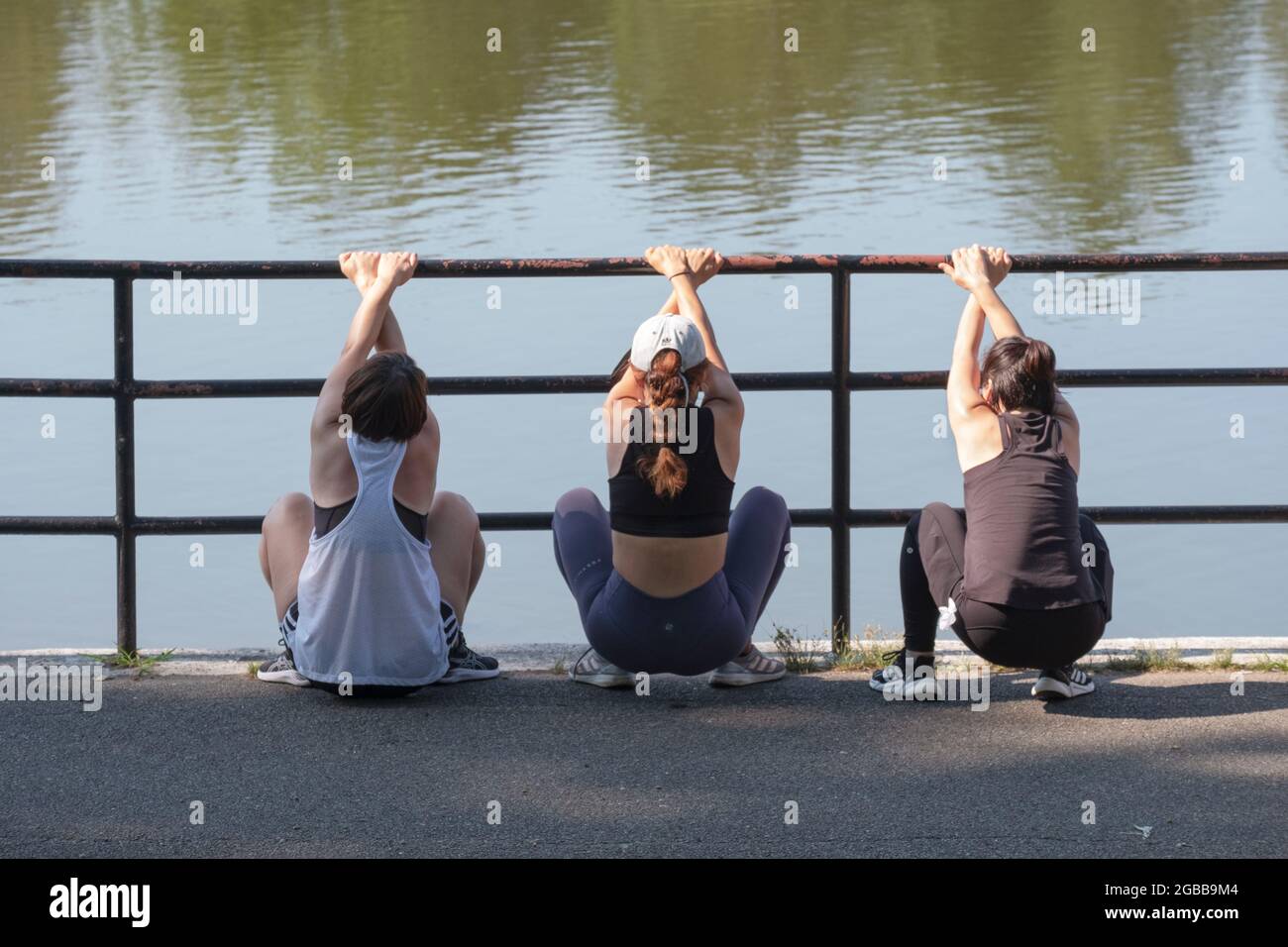 A very fit personal trainer, center, takes 2 clients through deep knee ...