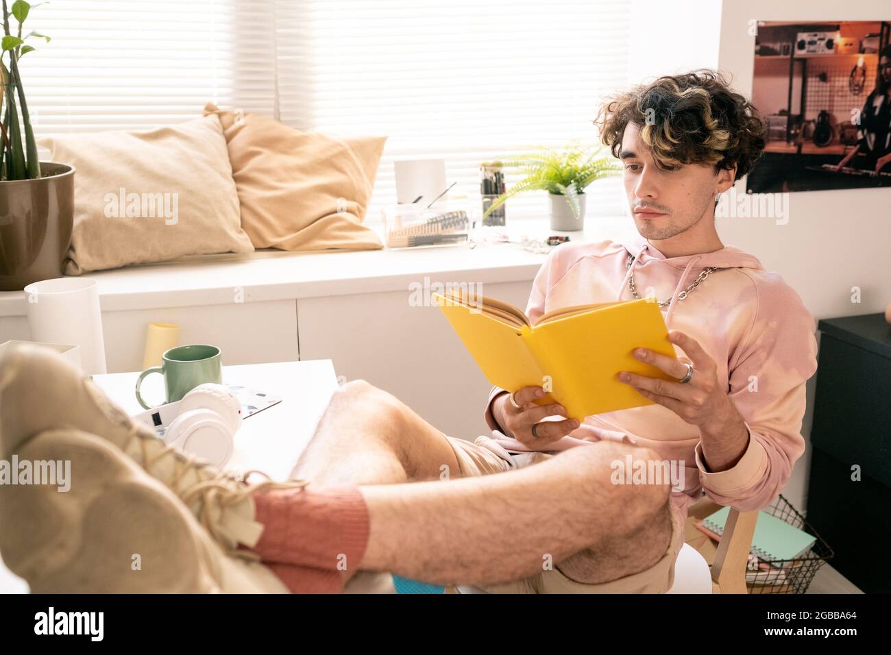 Restful teenager sitting on chair and reading book with his legs on ...