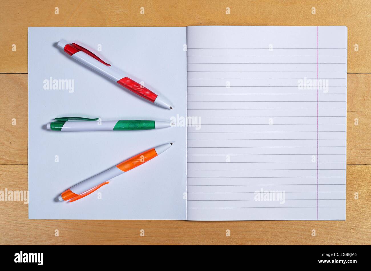 Three colored pens and opened school notebook on wooden desk, top view ...