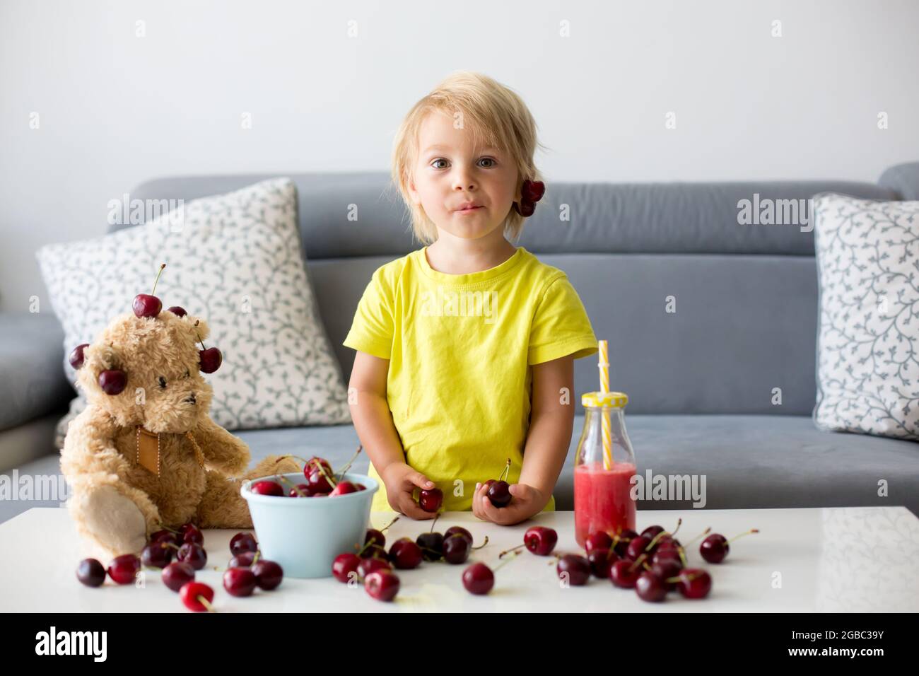 Toddler blond child, cute boy, eating cherries with teddy bears at home ...