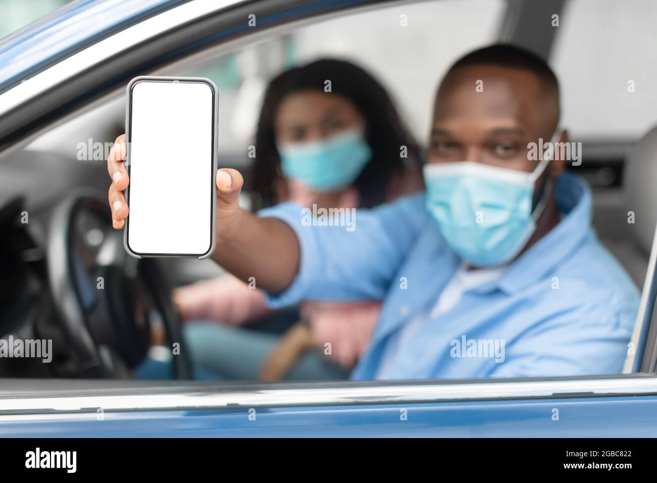 Driver in face mask using showing smartphone with empty screen Stock ...