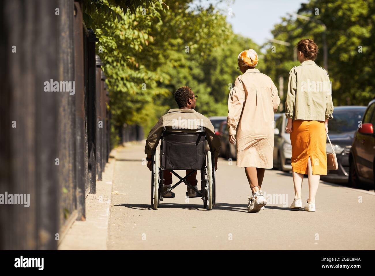 Rear view of handicapped black man in wheelchair walking with able ...