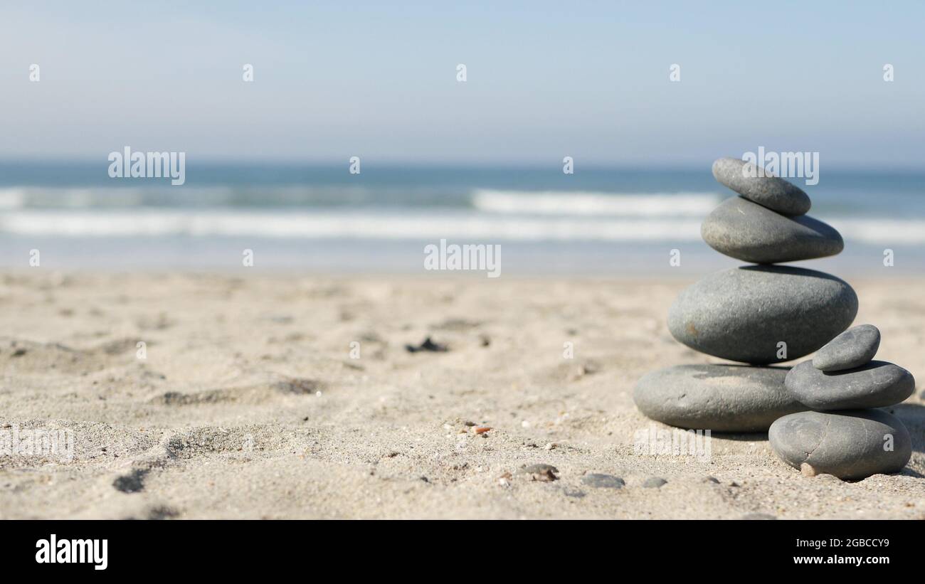 Rock balancing on ocean beach, stones stacking by sea water waves ...
