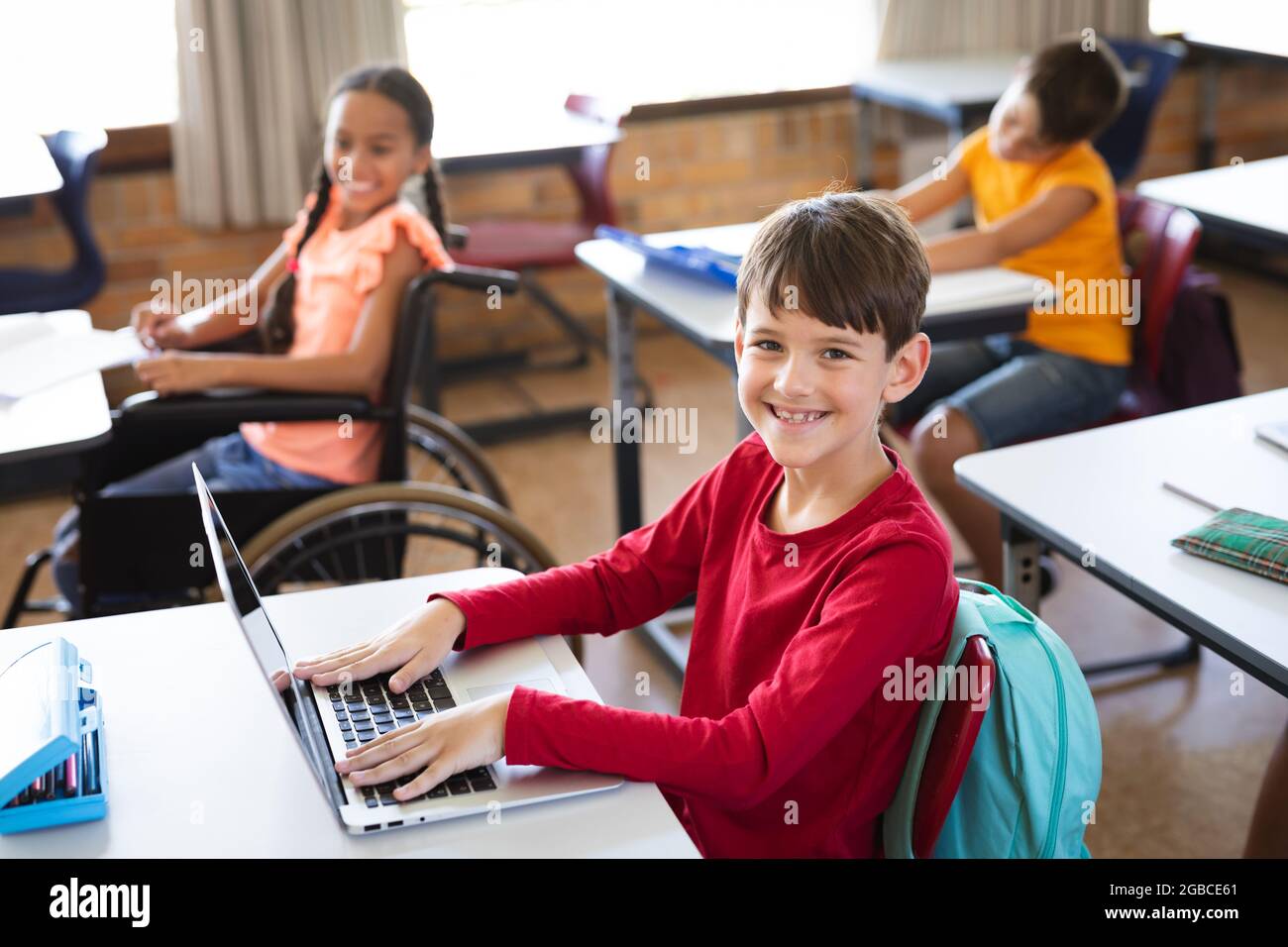 Portrait of caucasian boy with laptop smiling while sitting on his desk ...