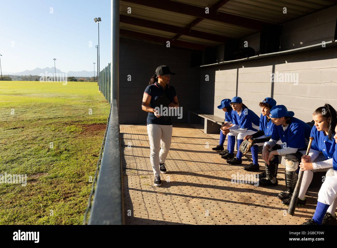 Diverse group of female baseball players sitting on bench, listening to ...