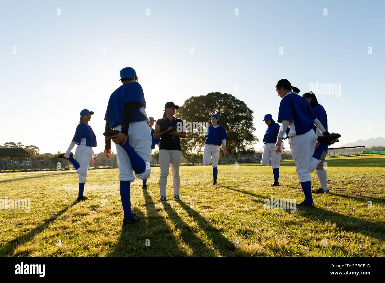 Diverse group of female baseball players with coach, warming up on ...