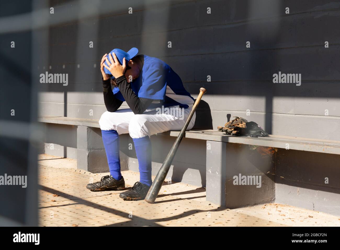 Mixed race female baseball player sitting on bench with head in hands ...