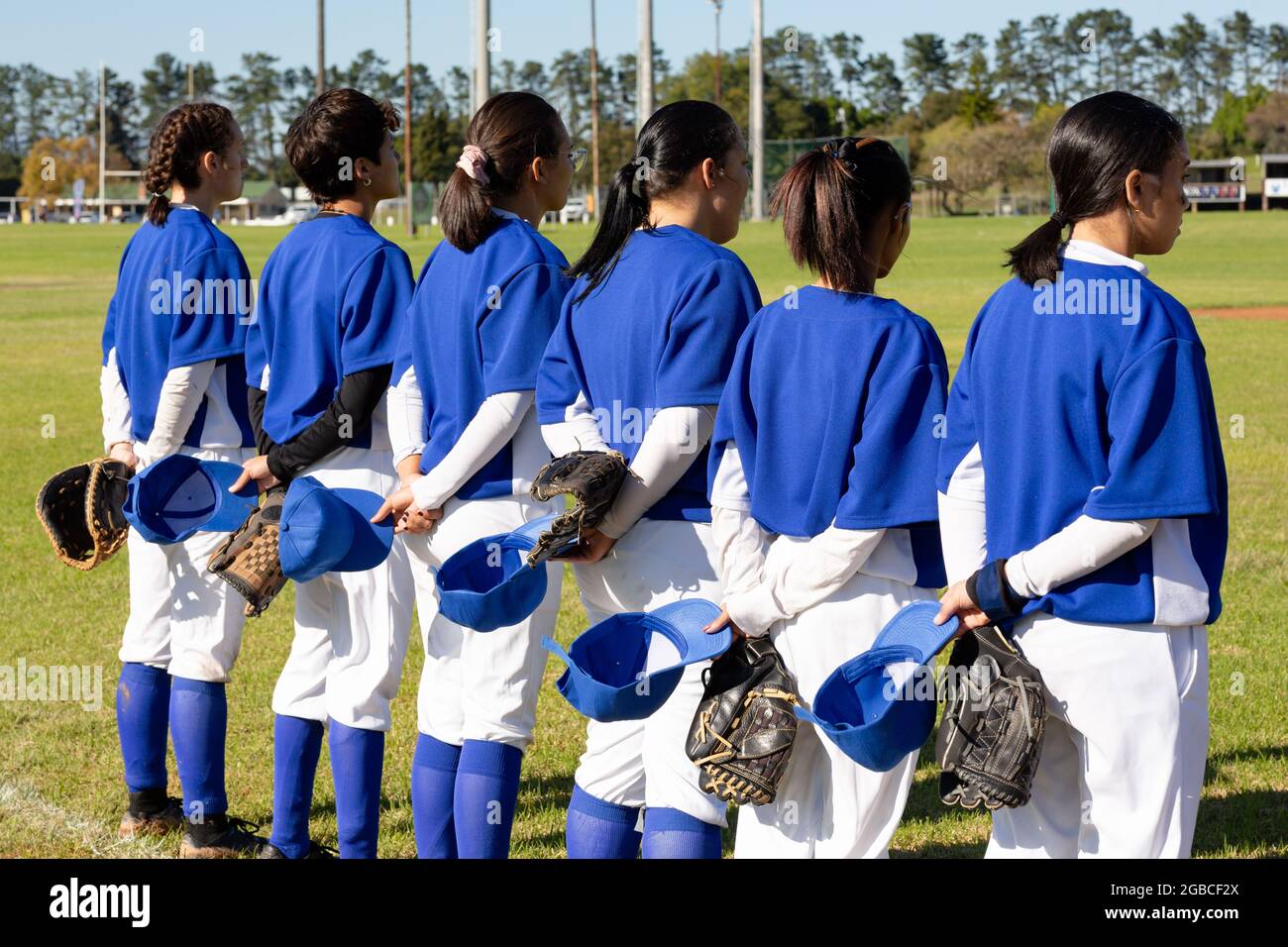 Diverse group of female baseball players standing on field with hands ...