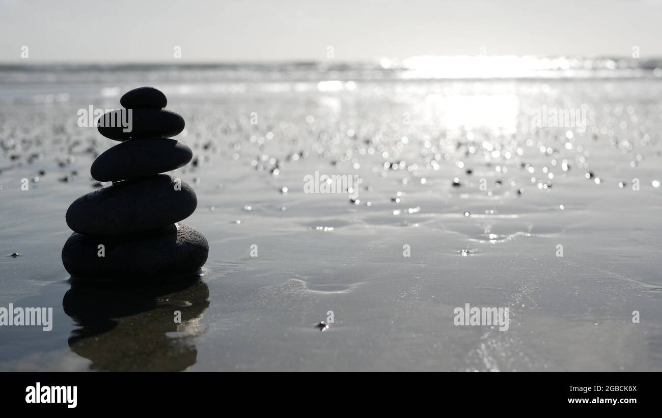 Rock balancing on ocean beach, stones stacking by sea water waves ...