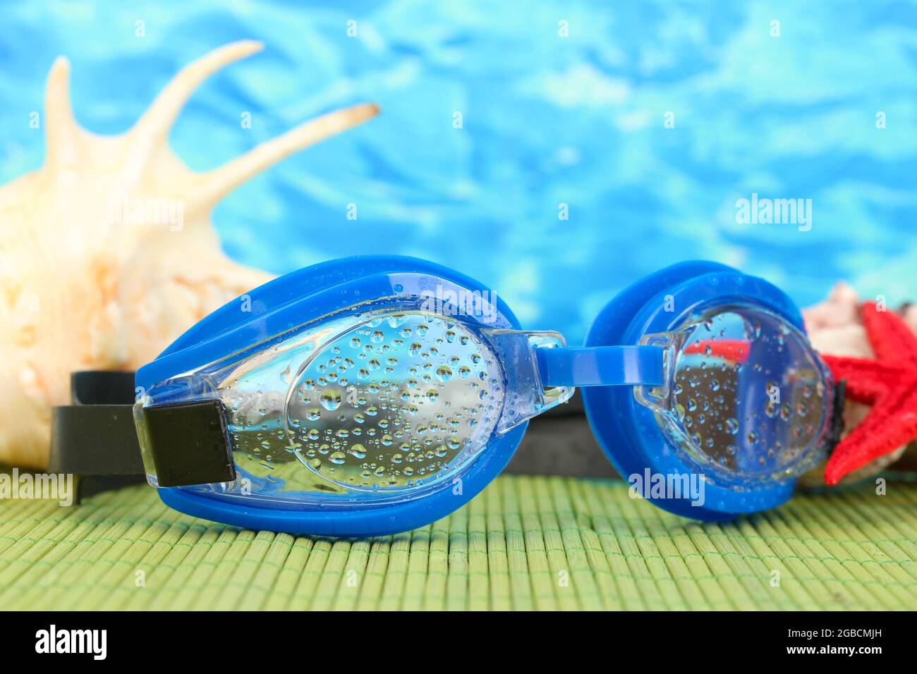 blue swim goggles with drops on a bamboo pad, on blue sea background ...