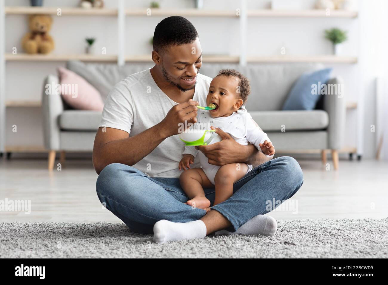 Caring Black Dad Feeding His Adorable Infant Baby From Spoon At Home ...