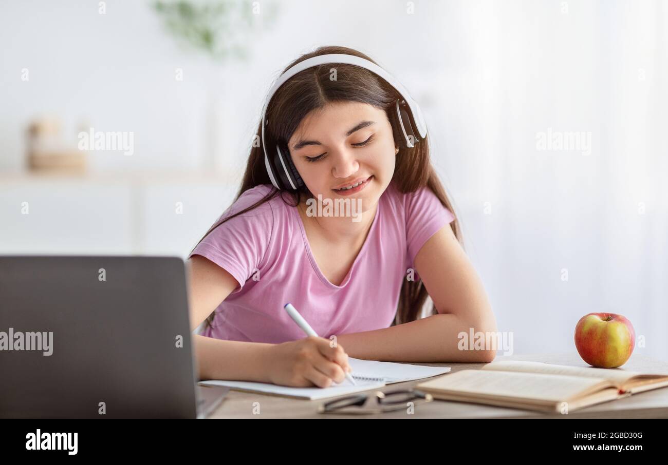 Home schooling. Joyful Indian teenage girl in headphones taking notes ...