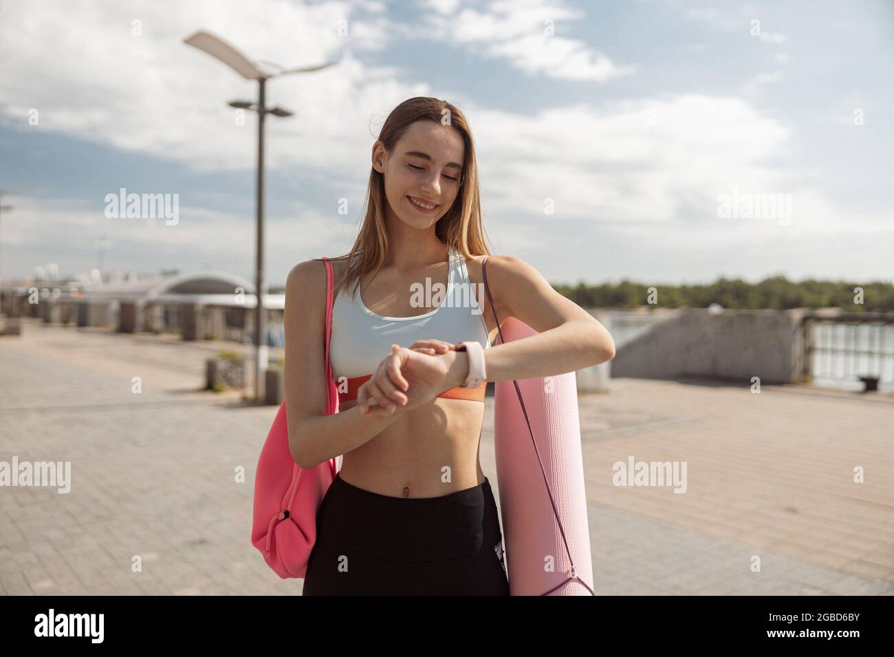 Cheerful athletic woman checks time on smartwatch standing on city ...