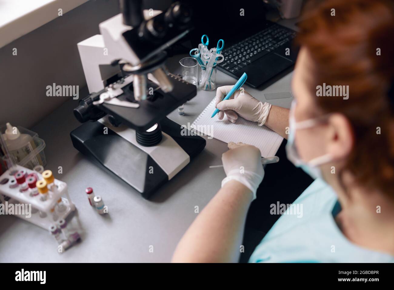 Female laboratorian writes notes in notebook near modern microscope at ...