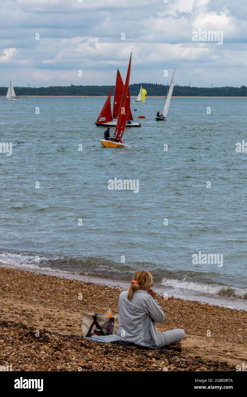 woman sitting alone on beach watching boats, lady sitting on shingle ...