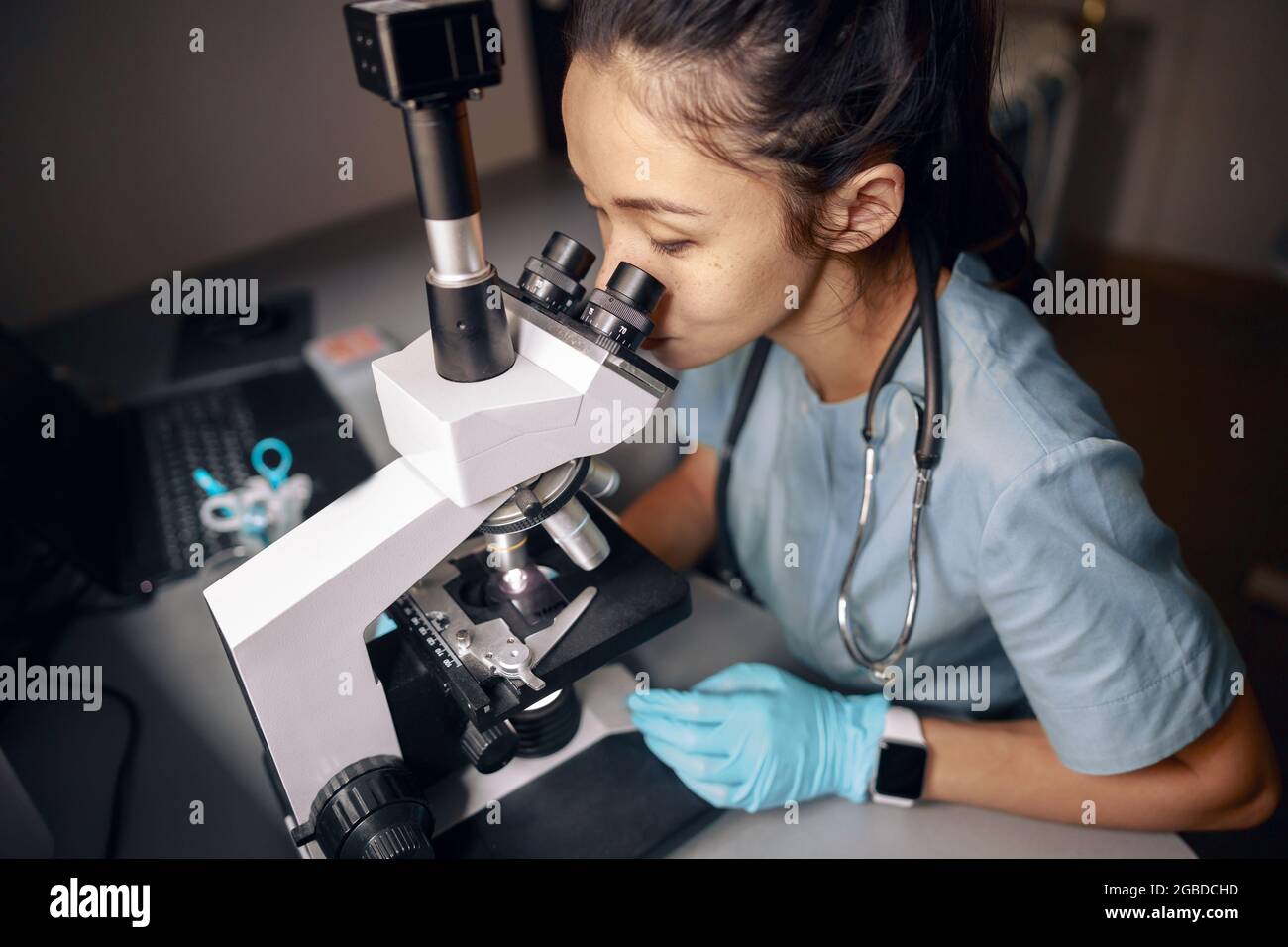 Asian lady lab assistant with stethoscope looks into microscope at ...