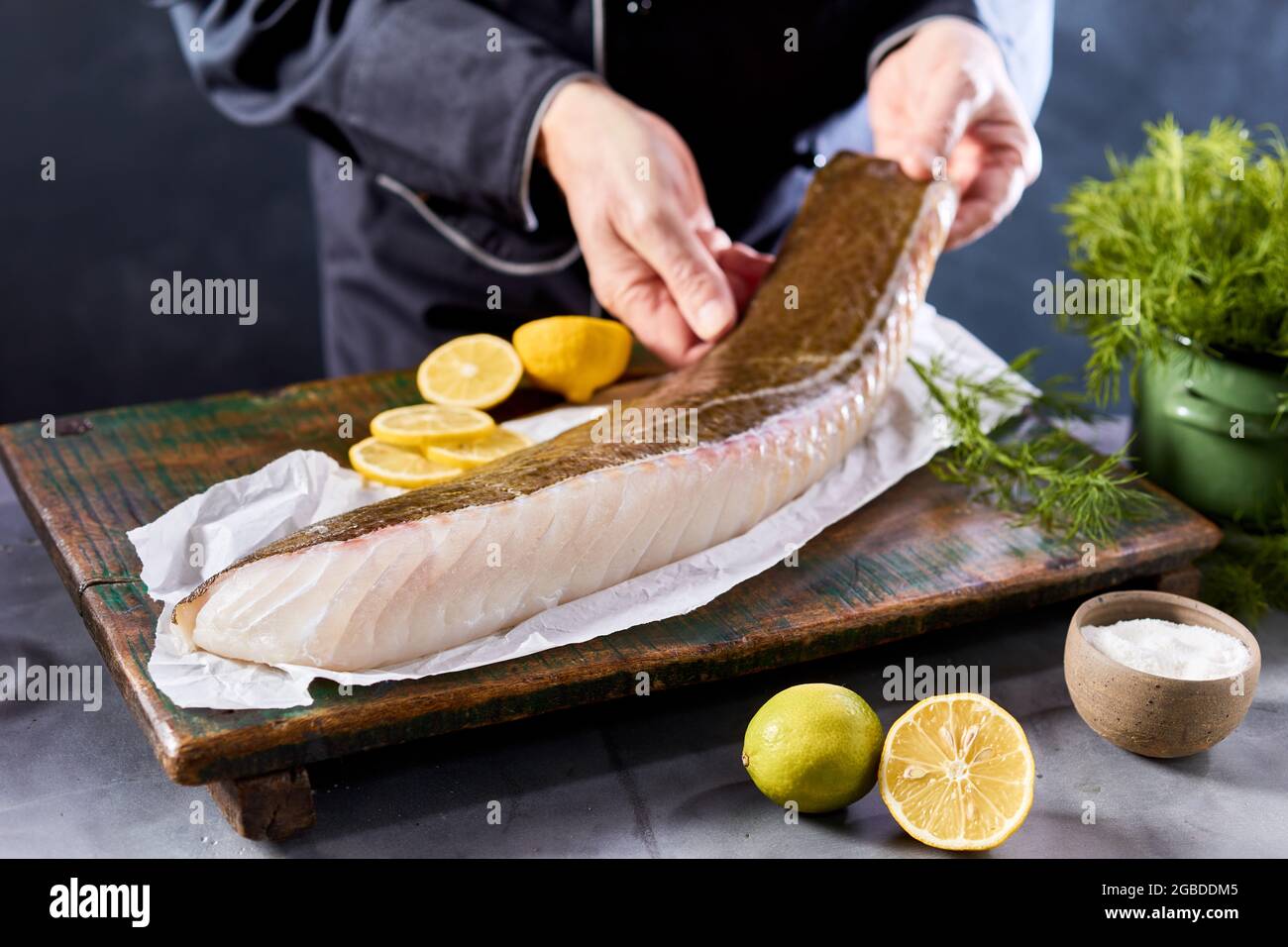 Crop unrecognizable cook in black uniform placing uncooked fresh cod ...