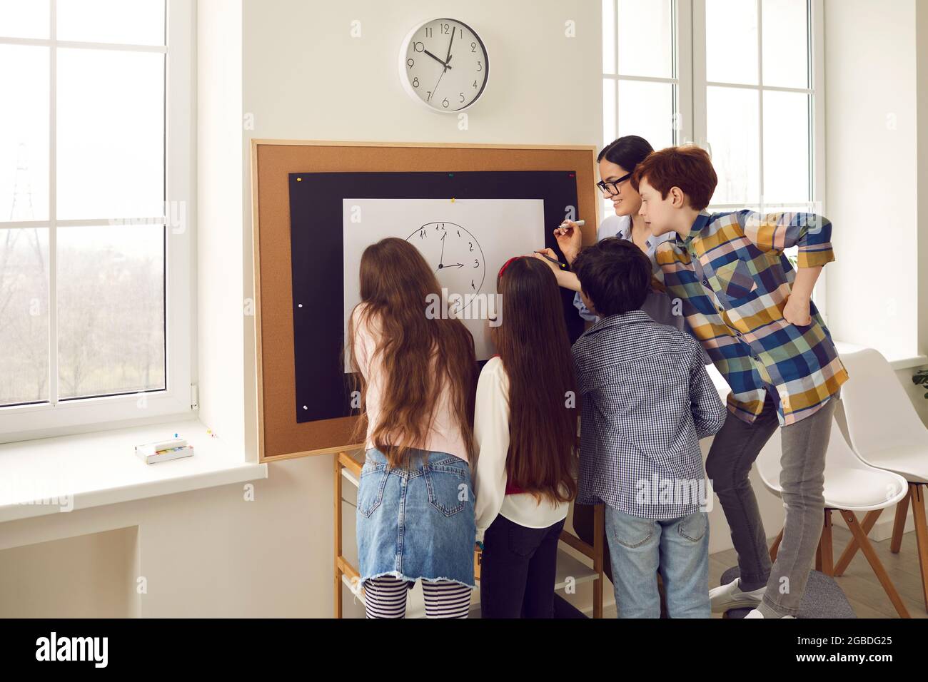 Teacher teaching schoolchildren group reading clock time, minutes and ...