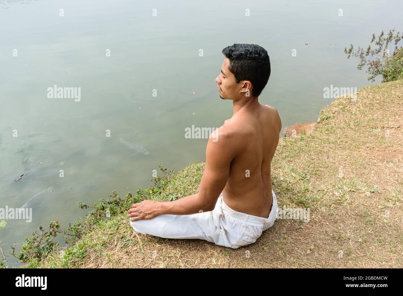 Brazilian young man sitting looking at the lake in meditation position ...