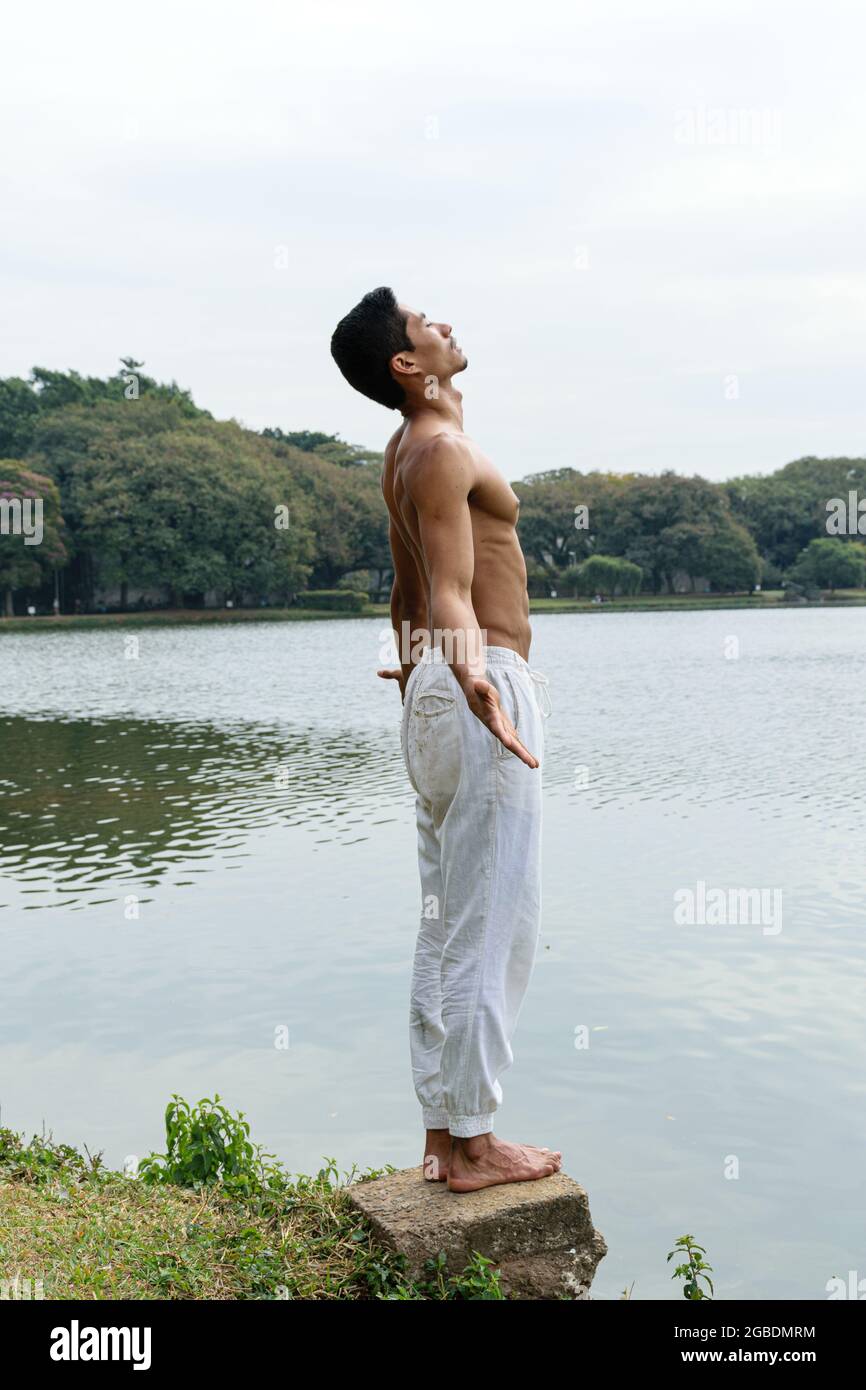 Brazilian young man standing beside a lake with his arms open and ...