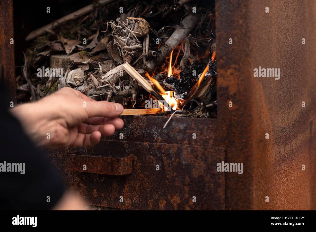 Male hand making a fire with small wooden branches in a outdoor rusty ...