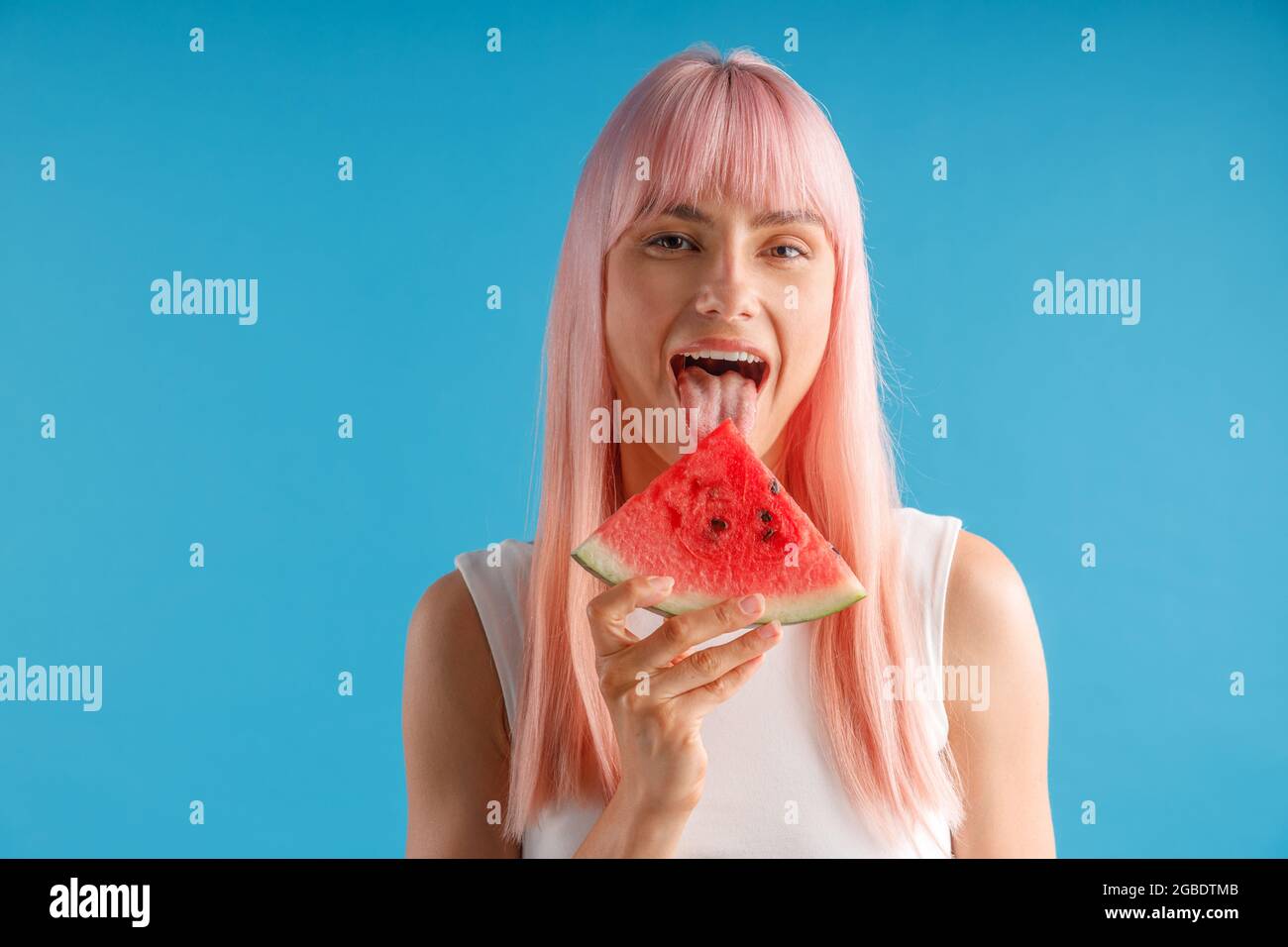 Playful young woman with pink hair holding a slice of watermelon ...