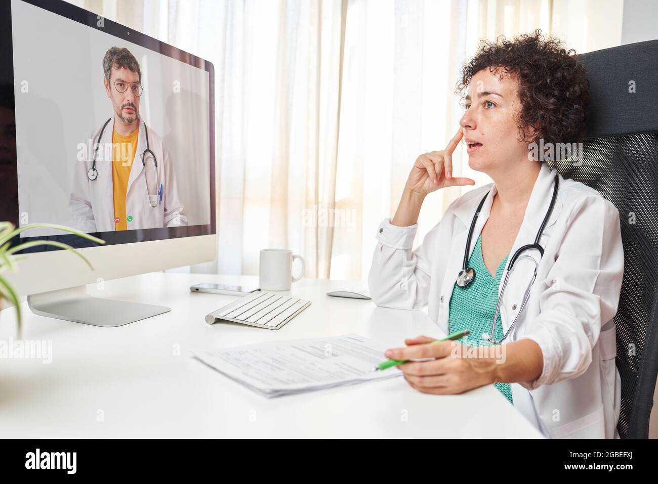 Healthcare worker talking to coworker on video call over computer while ...