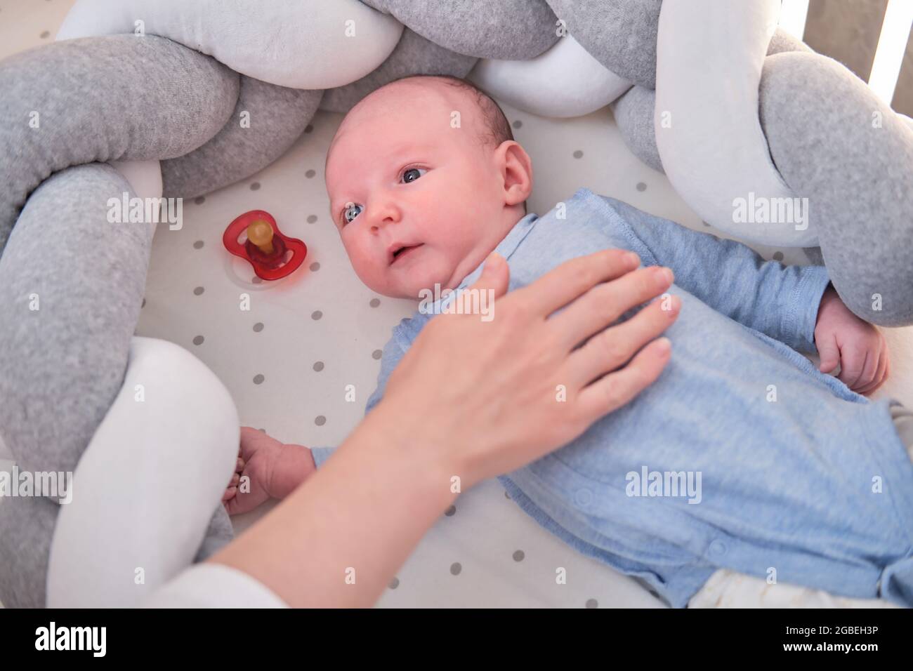 Mom strokes a newborn baby with her hand in the crib, child boy aged 1 ...