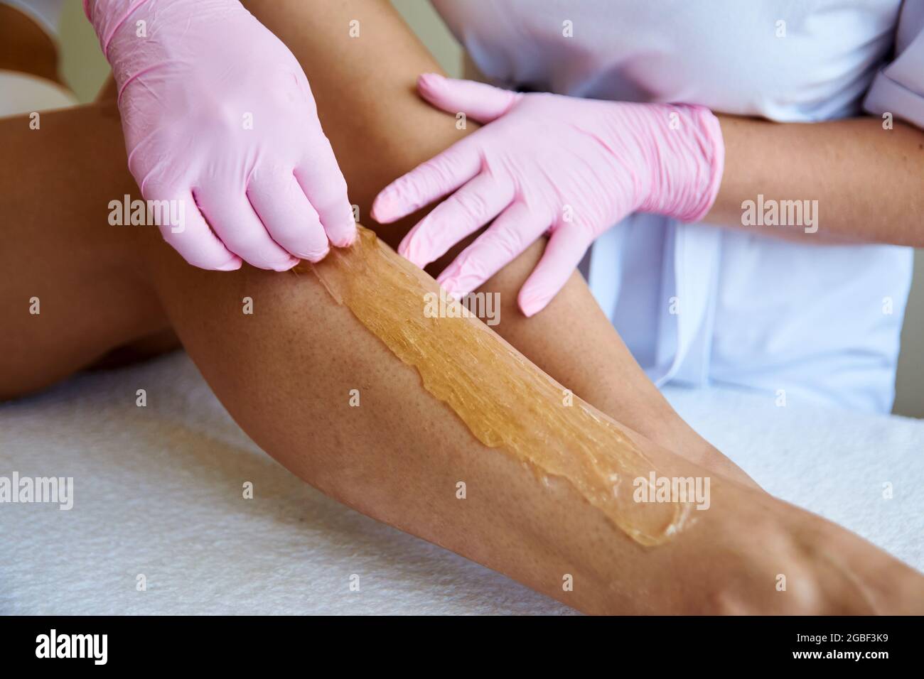 Lovely young beautician applies sugar paste to the client's leg. Hair ...