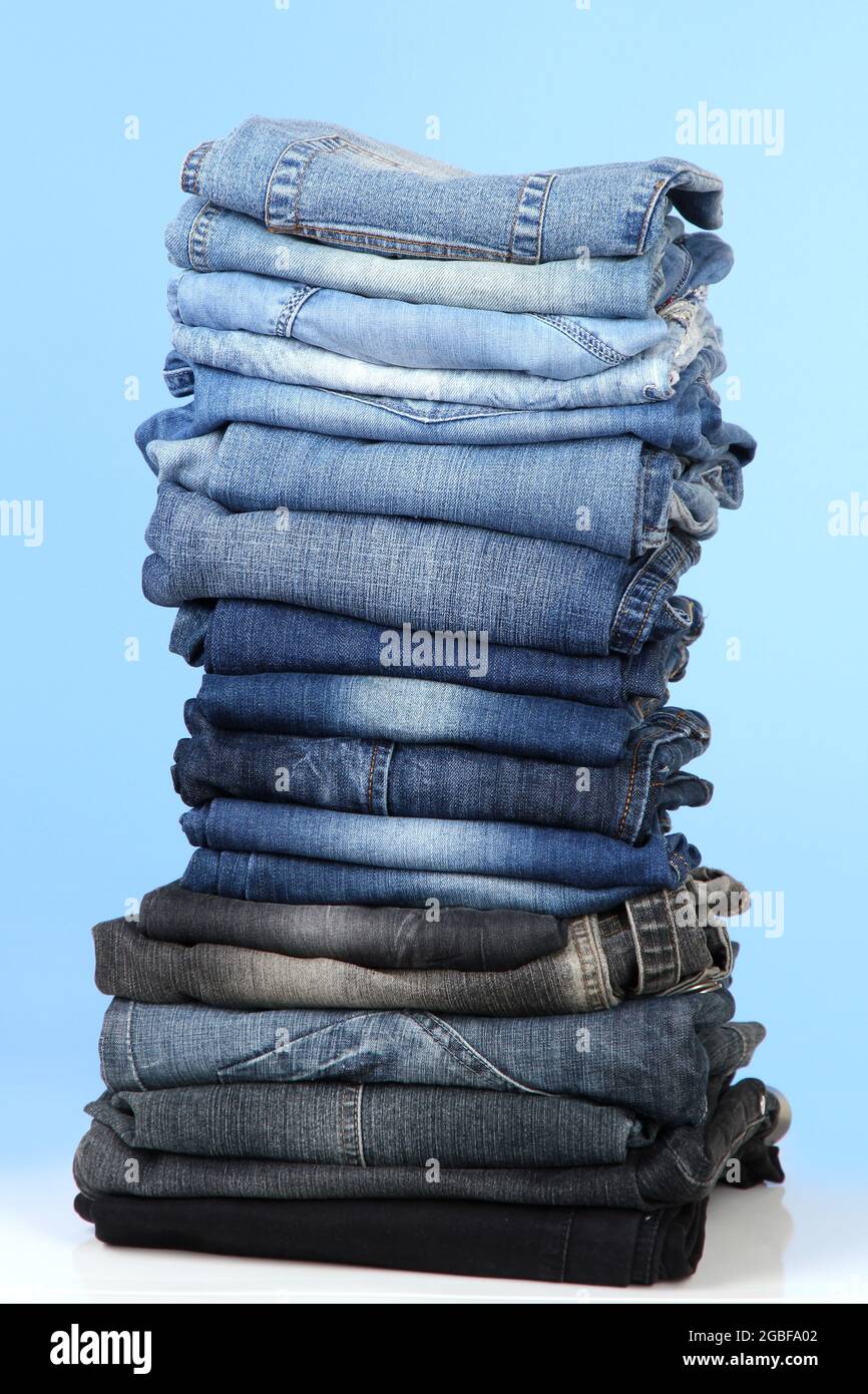 Many jeans stacked in a pile on blue background Stock Photo - Alamy