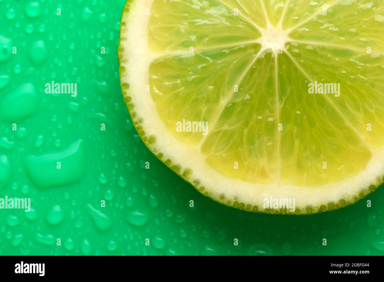 Slice of lime with drop on green background Stock Photo - Alamy