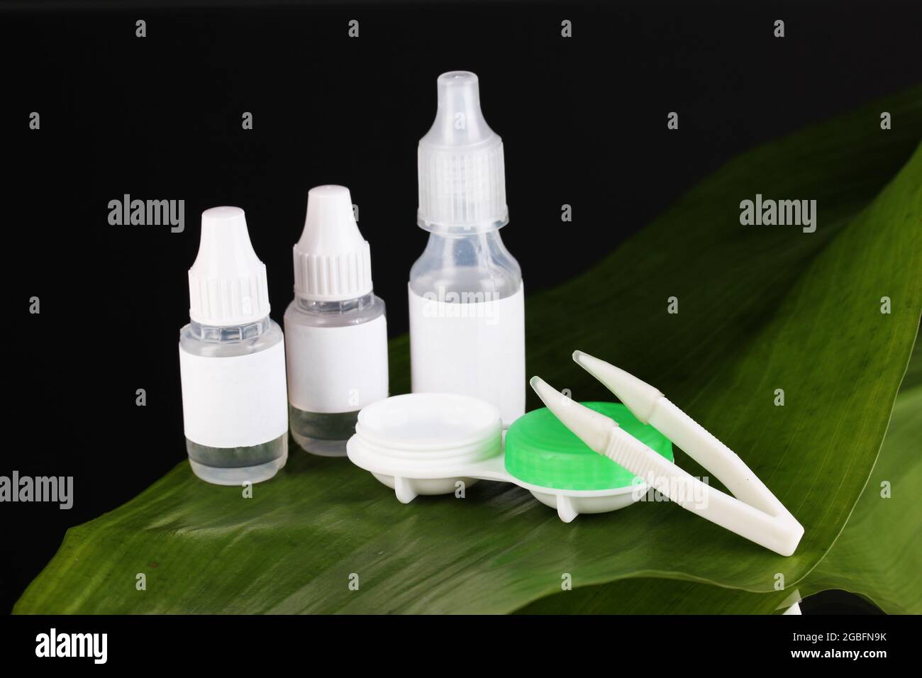 Eye drops and lenses on leaf on black background Stock Photo - Alamy