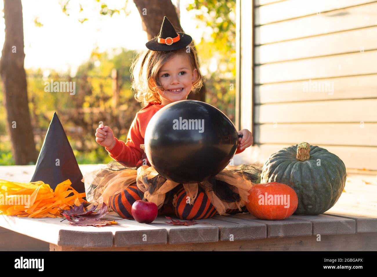 A cute little girl 2-3 in an orange and black witch costume sits next ...