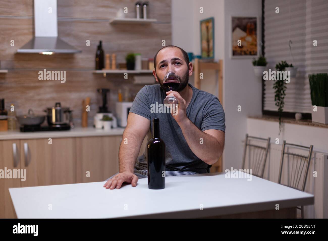 Pensive man drinking glass of wine while sitting alone and depressed ...