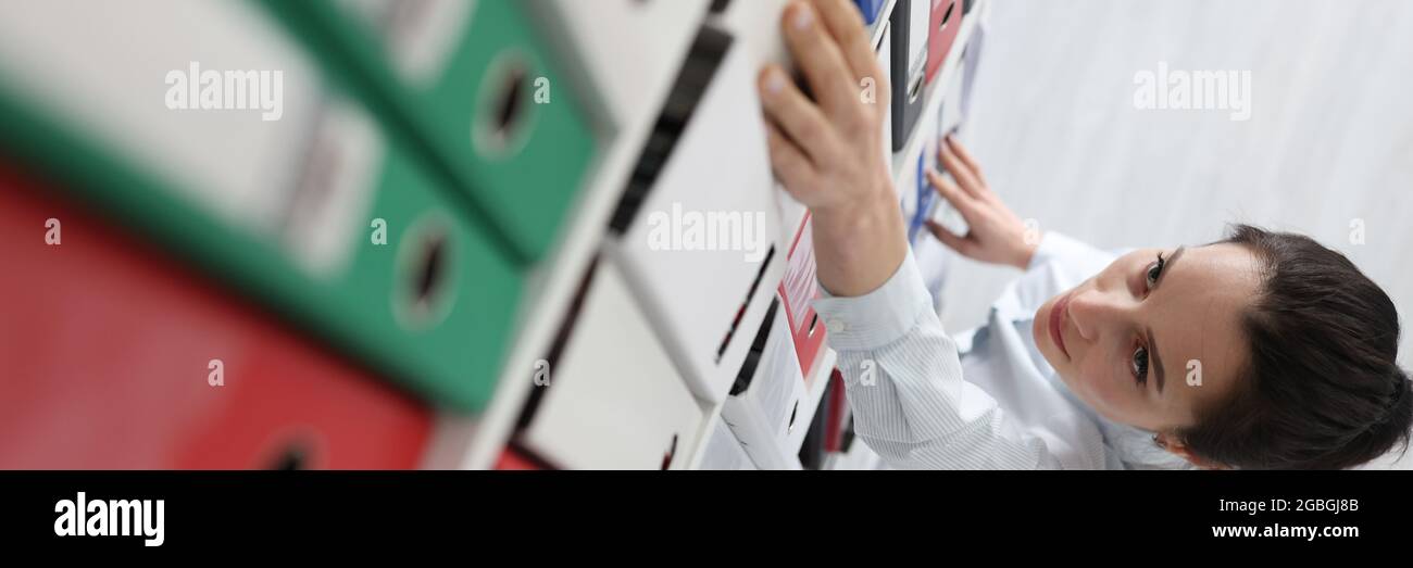 Woman pulling out folder with documents from top shelf Stock Photo - Alamy