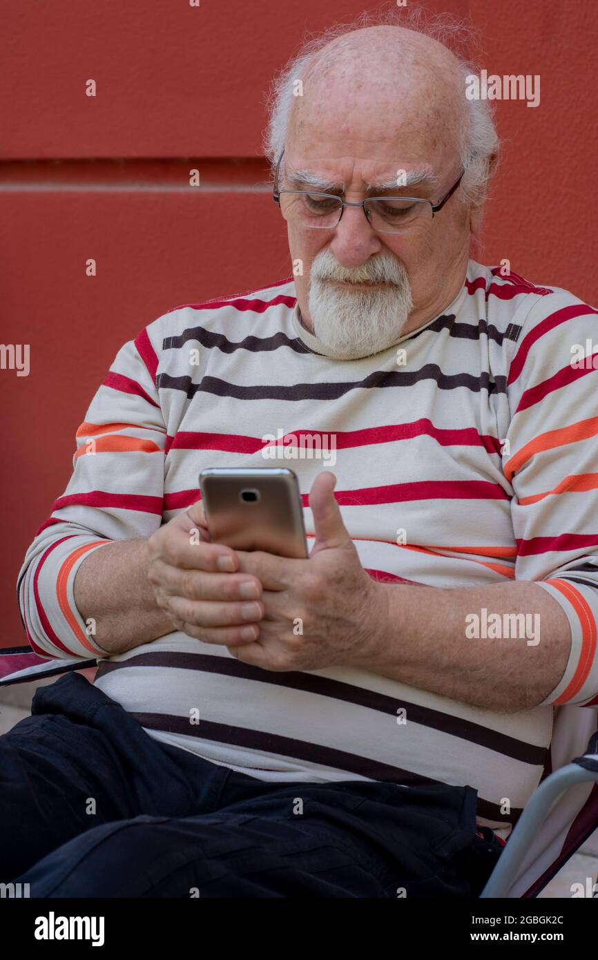old man sitting in front of his house, dealing with his cell phone. can ...