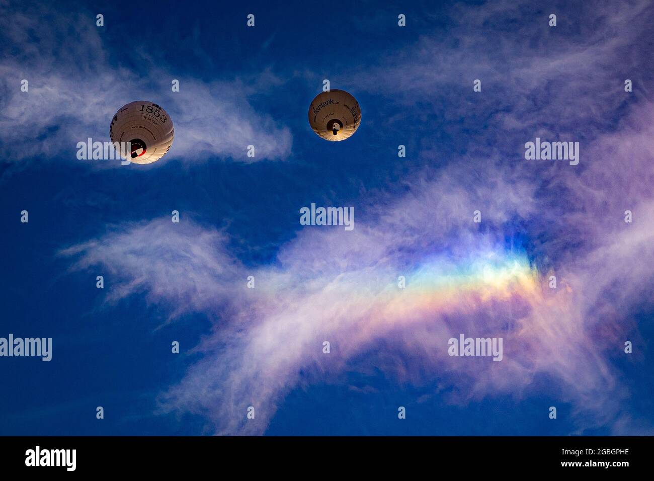 Hot air balloons pass by colourful cloud irisation, an optical ...