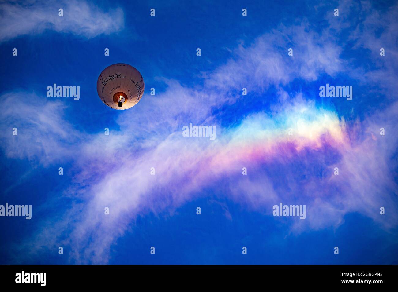 A hot air balloon passes by colourful cloud irisation, an optical ...