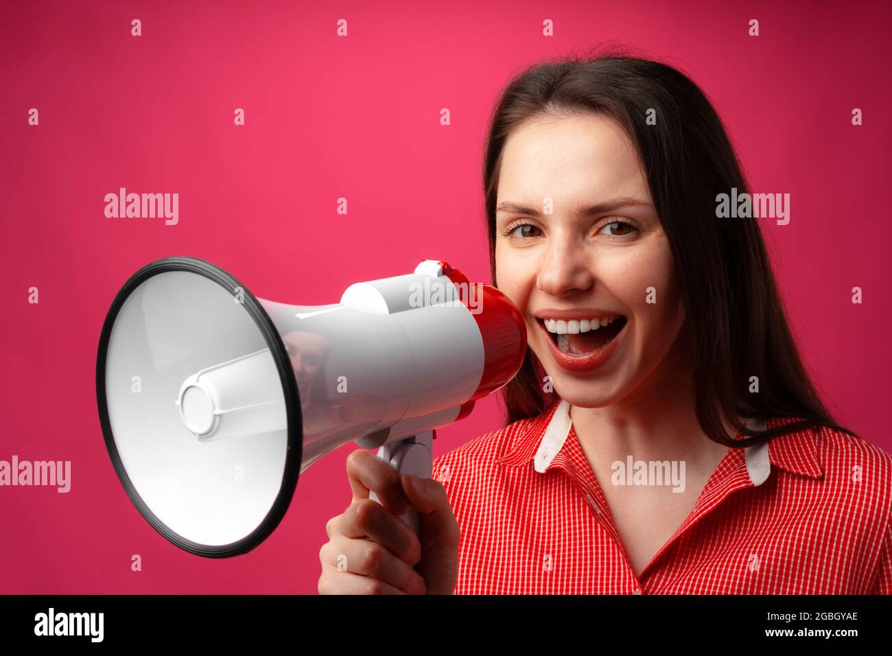 Young brunette woman shouting in megaphone against pink background ...